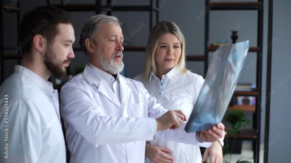 Vidéo Stock Three adult and young doctors examining X-ray scan together ...