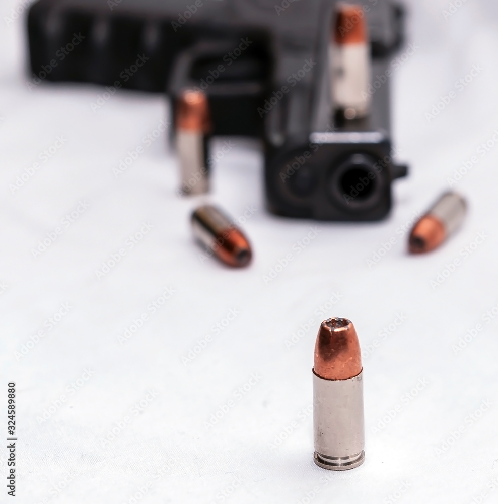 A single 9mm hollow point bullet in front of a black 9mm pistol ...