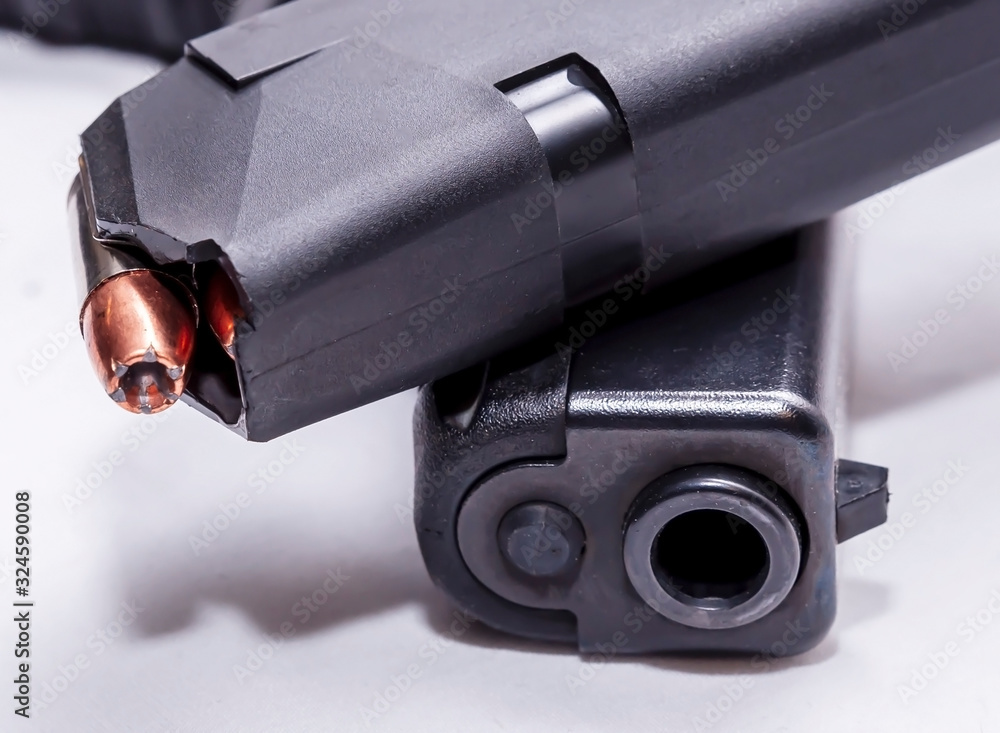 A black 9mm pistol with a pistol magazine loaded with 9mm hollow point bullets on a white ...