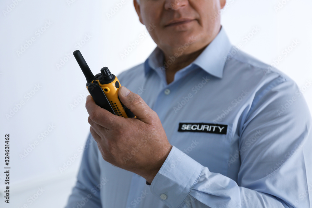 Professional security guard with portable radio set on light background ...