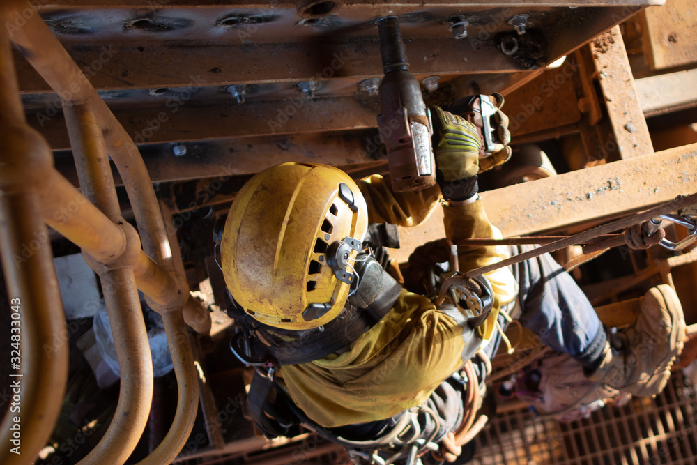 Rope access construction worker working in fall arrest position wearing ...