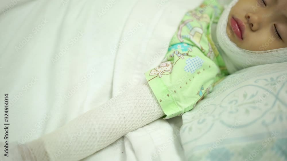 Asian baby girl lying sick with bandaged head and arm on bed at ...