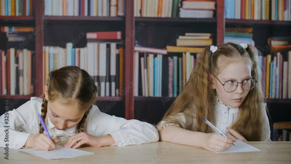 Worried small girl cribbing from paper during exam. Little schoolgirls ...