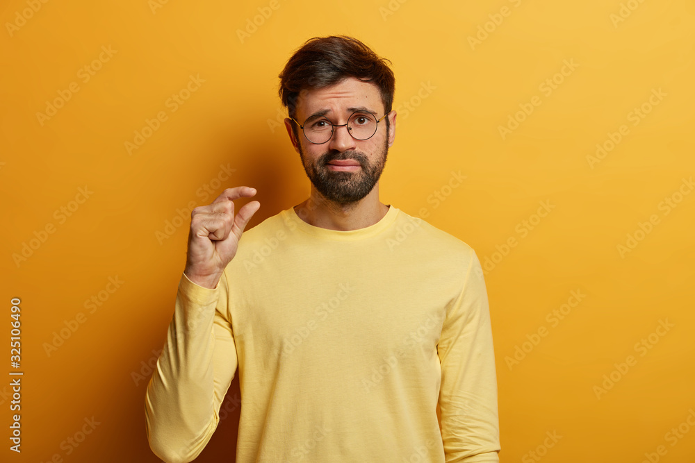 Disappointed adult man shows small size, measures something very tiny ...