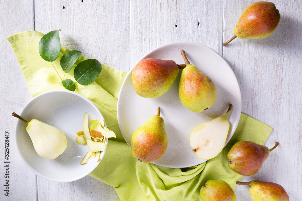 Ripe pears on a light bowl with leaves on a white wooden background ...