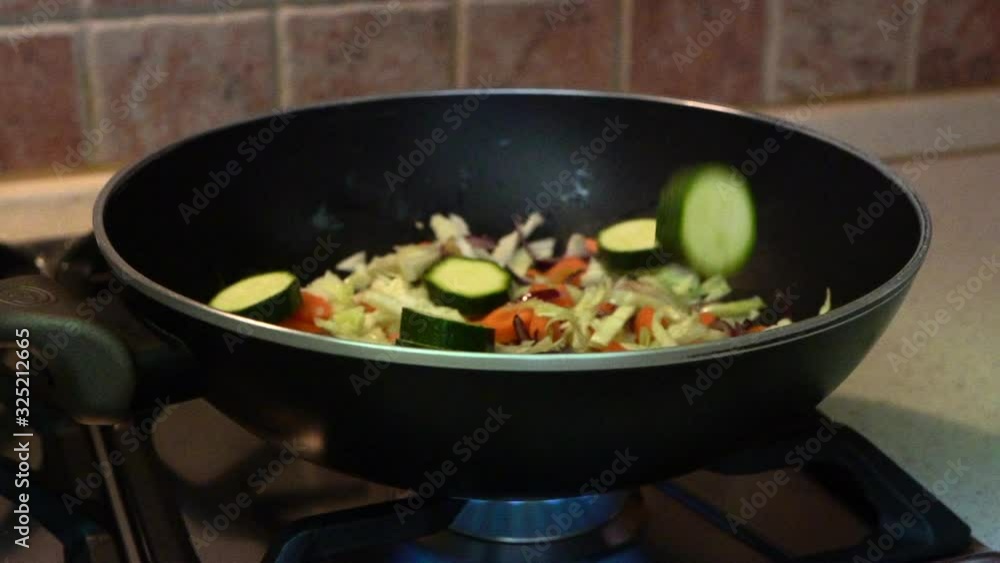 Fresh cut vegetables falling in cooking pan and mixing for frying on ...