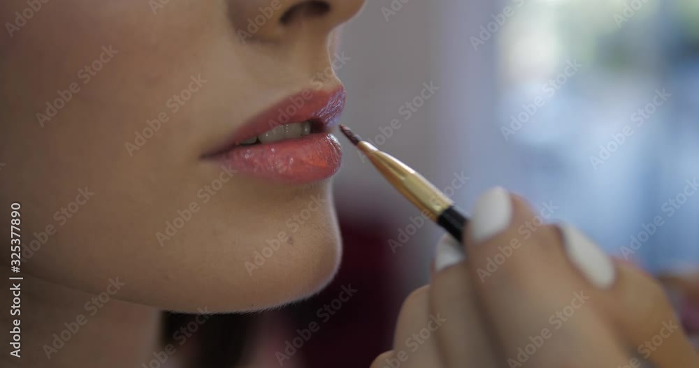 experienced beauty salon worker applies pink lipstick on beautiful ...