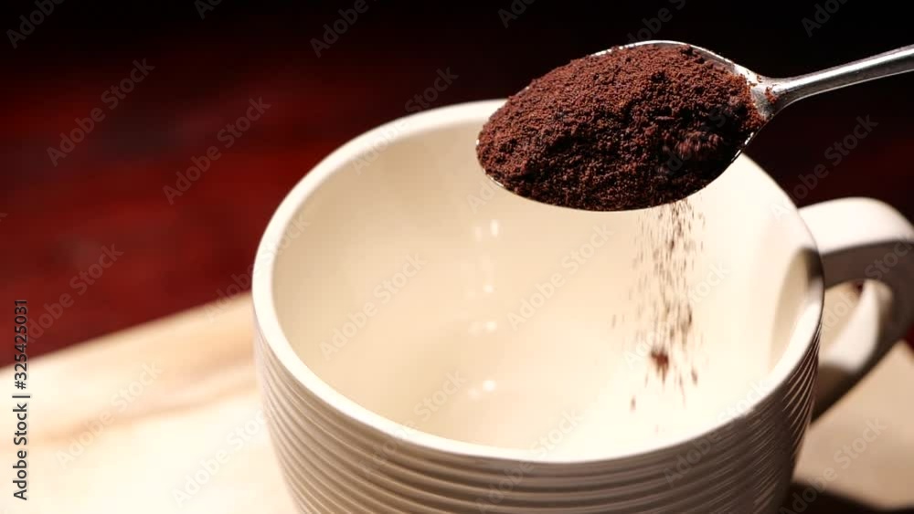 Pouring Coffee powder from tea spoon into a white cup in slow motion ...