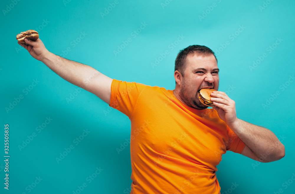 Emotional happy fat man on a blue background eating fast food ...