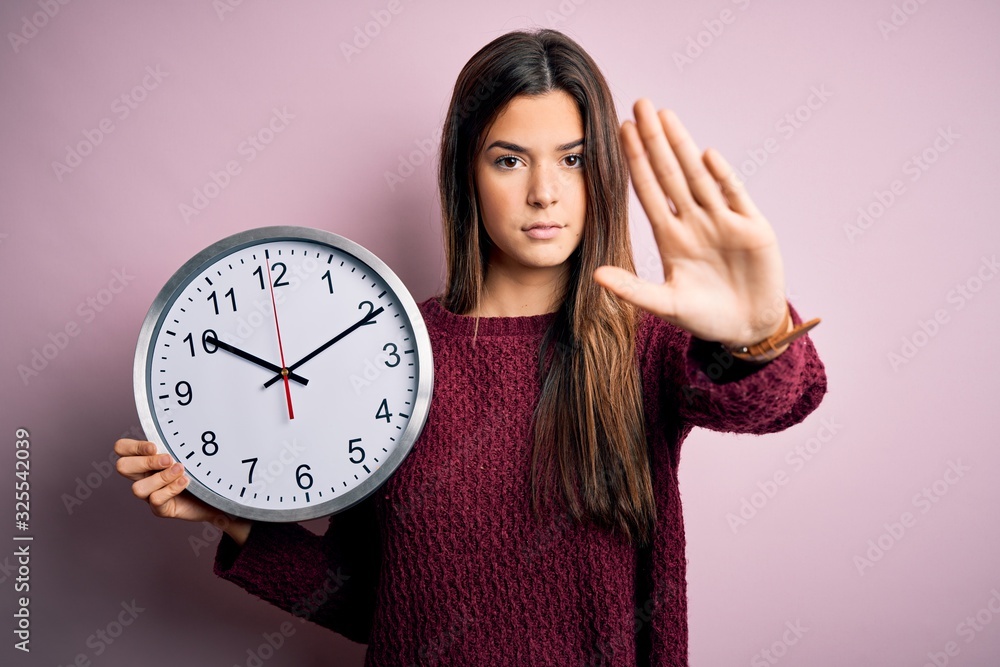 Young beautiful girl doing countdown holding big clock over isolated ...