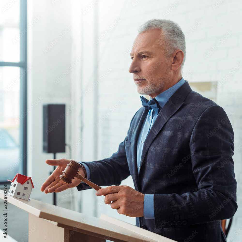 auctioneer pointing with hand at model of house and holding gavel ...