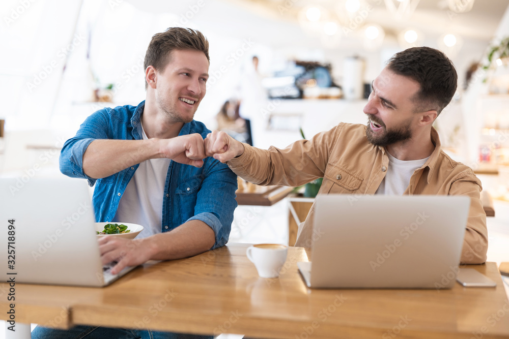 two colleagues men bumping their fists looking happy and winning during ...