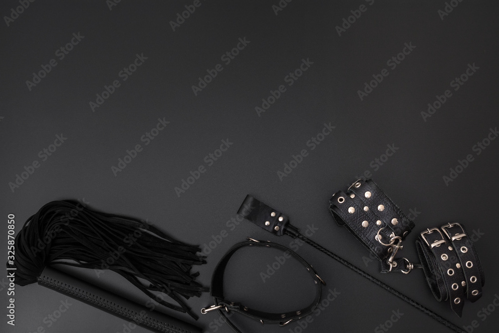Leather handcuffs, black whip, collar and stack on black background ...