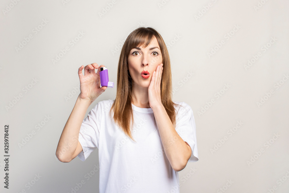young woman holds an inhaler in her hand with a surprised face on a ...