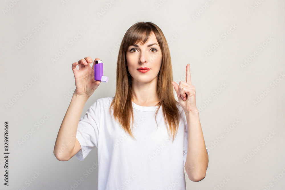young woman holds in her hand an inhaler, holding thumbs up on a light ...