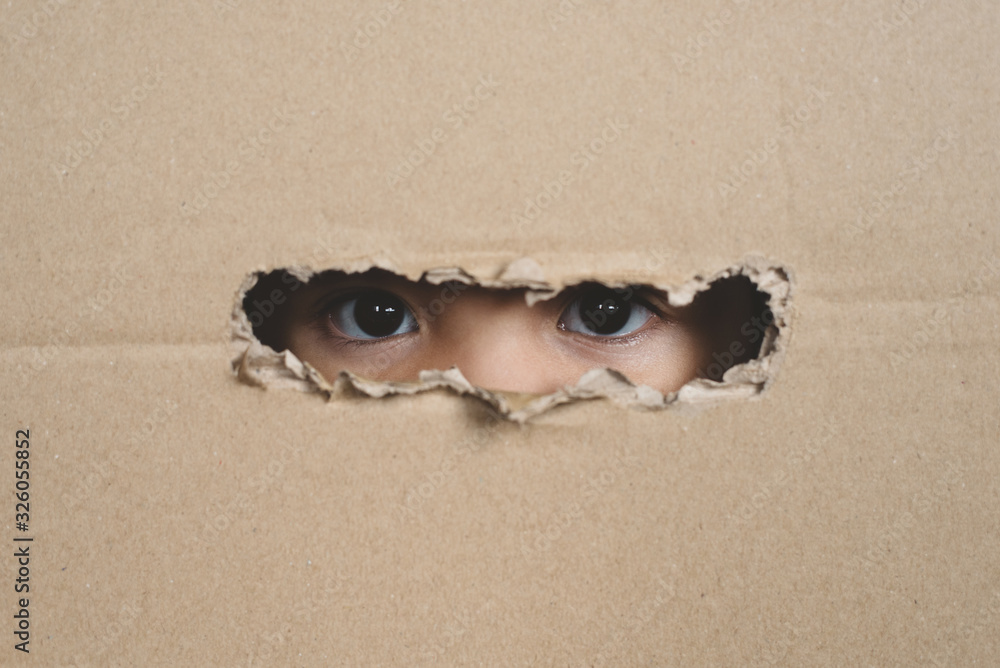 A child eye looking through a hole on a cardboard box. Concept of spy ...