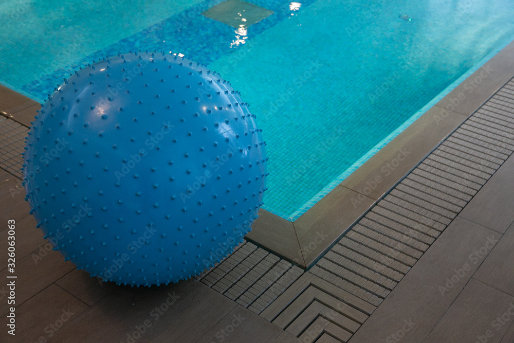blue gymnastic ball on the wooden side of an indoor pool with blue ...