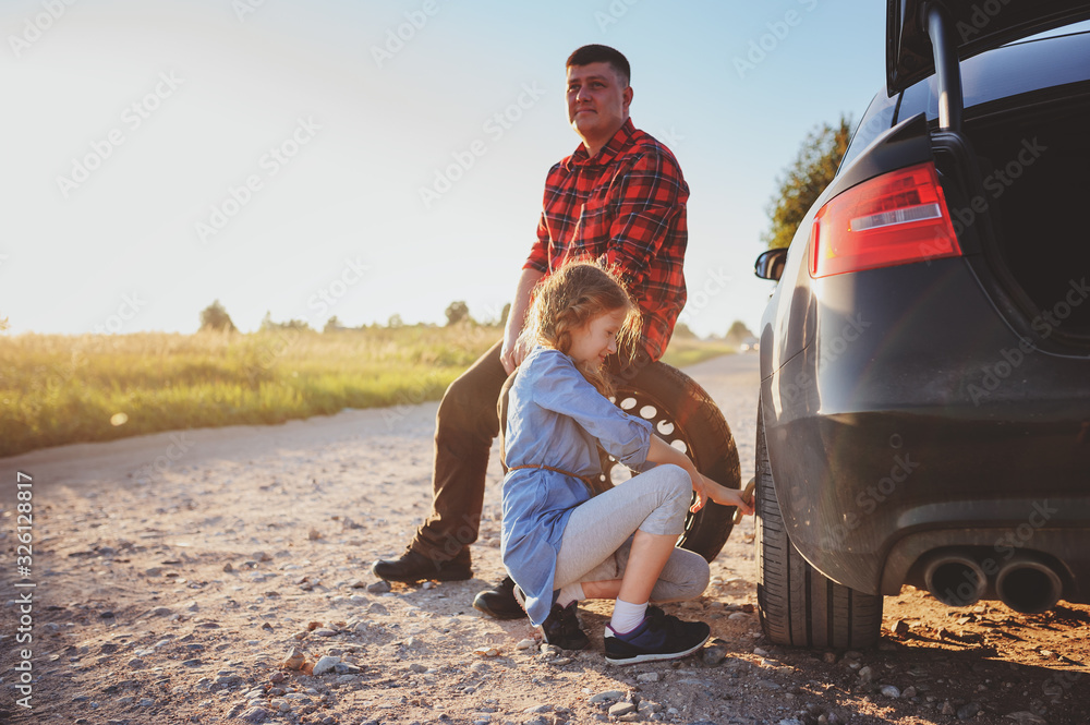father and daughter changing broken tire during summer rural road trip ...