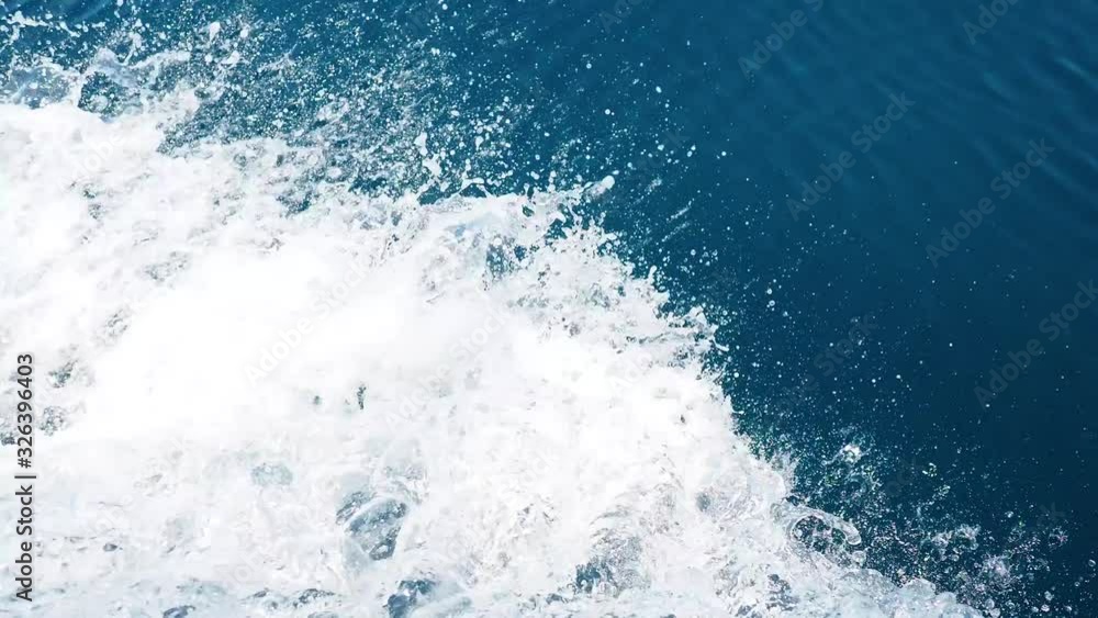 Ocean waves and splash from the side of a traveling cruise ship. Blue ...