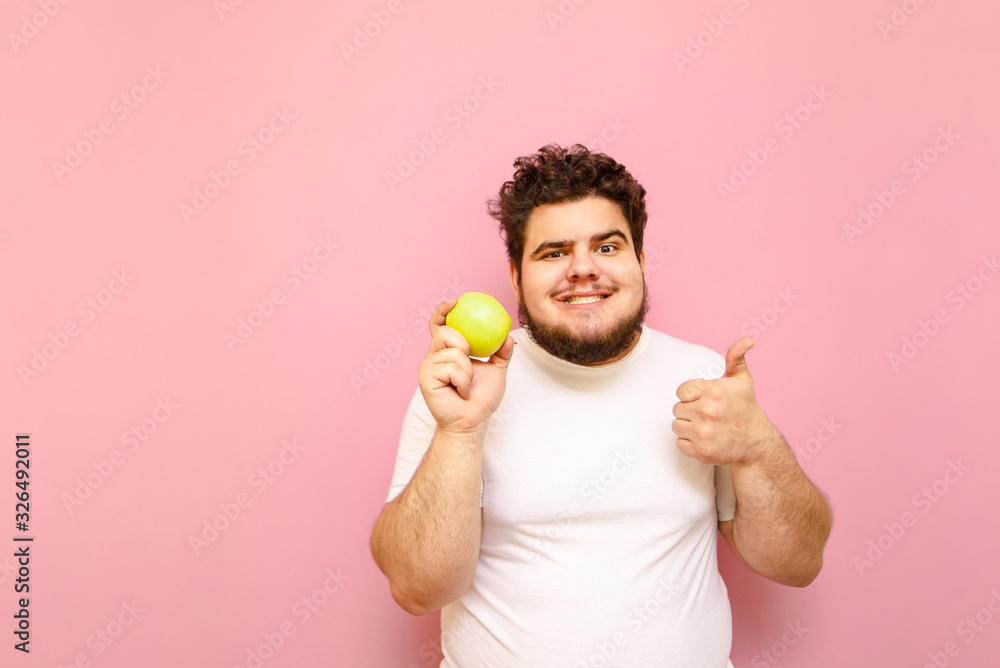 Funny bearded fat man in a white T-shirt stands with an apple in his ...