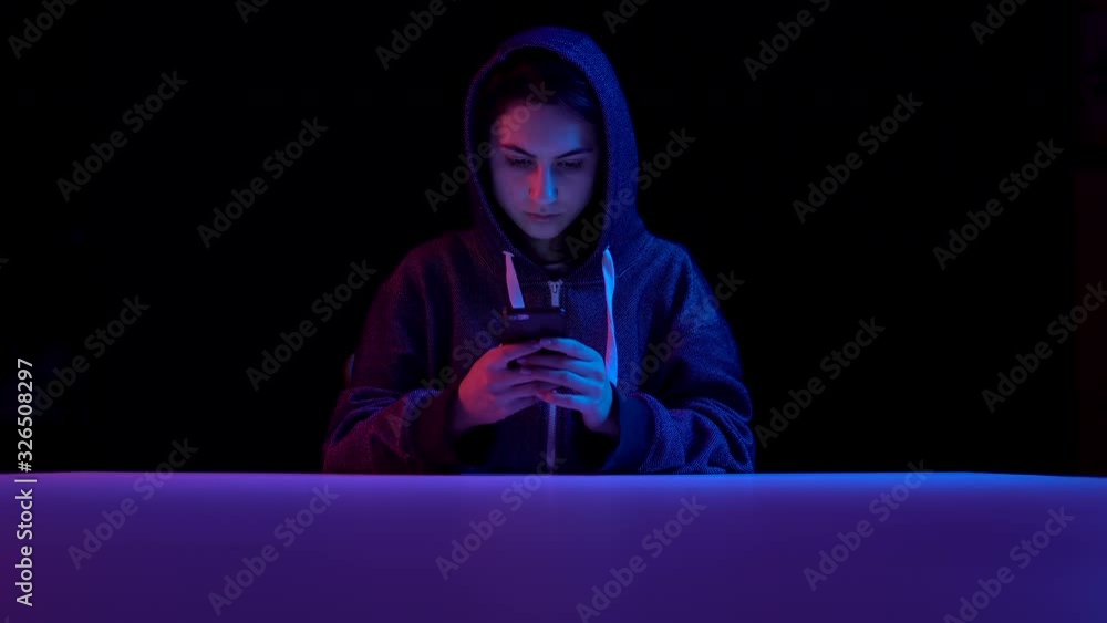 Young woman in a hood with a smartphone. Hacker makes a hack through ...