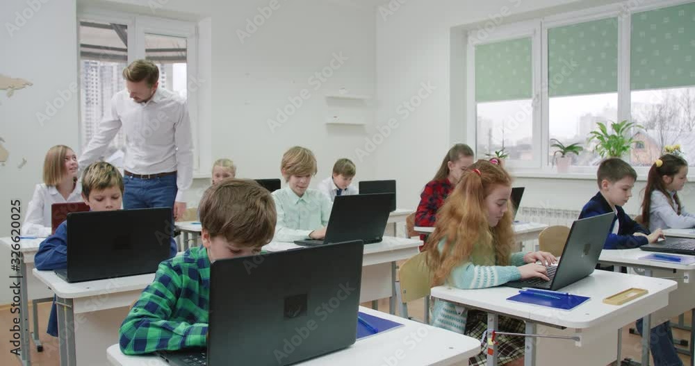 Education in the modern school, children use laptops, teacher monitors ...