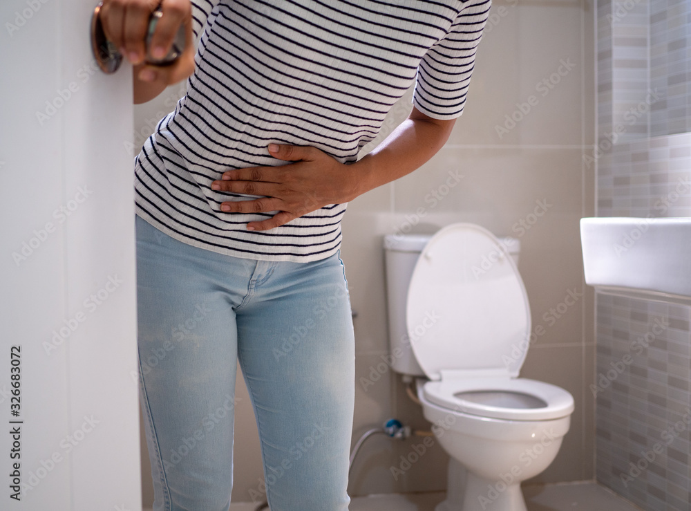 Woman with diarrhea standing in the bathroom, holding her stomach ...