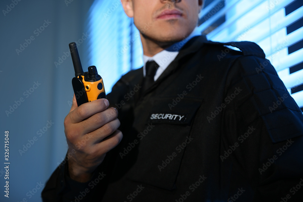 Professional security guard with portable radio set near window in dark ...