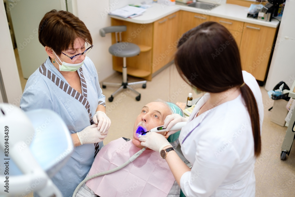 Doctor dentist and assistant doing dental operation of senior man 70-75 ...