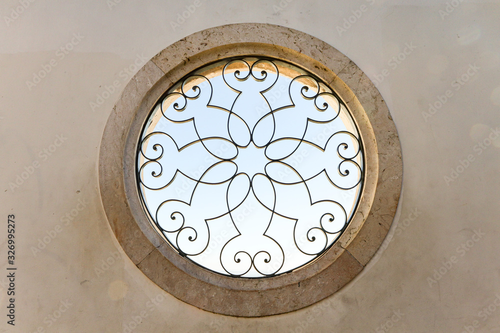 Round window with a black metal fence and a pattern in an old stone ...