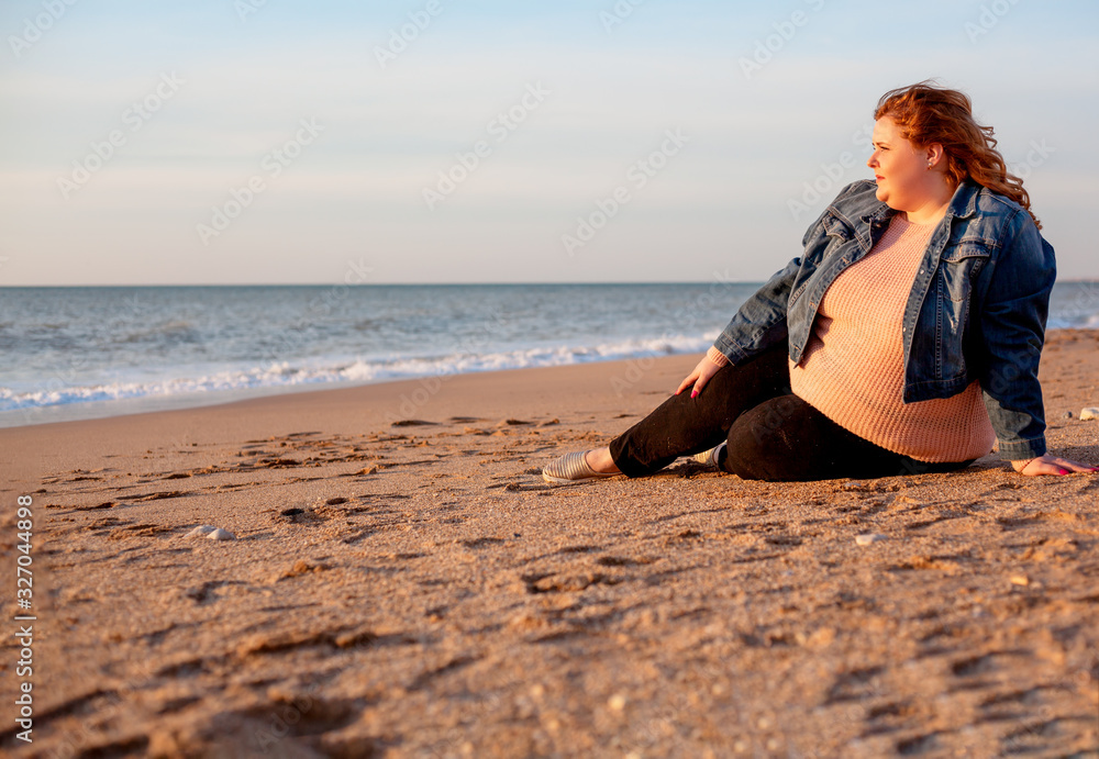 Back view of beautiful overweight woman sitting on the sandy beach ...