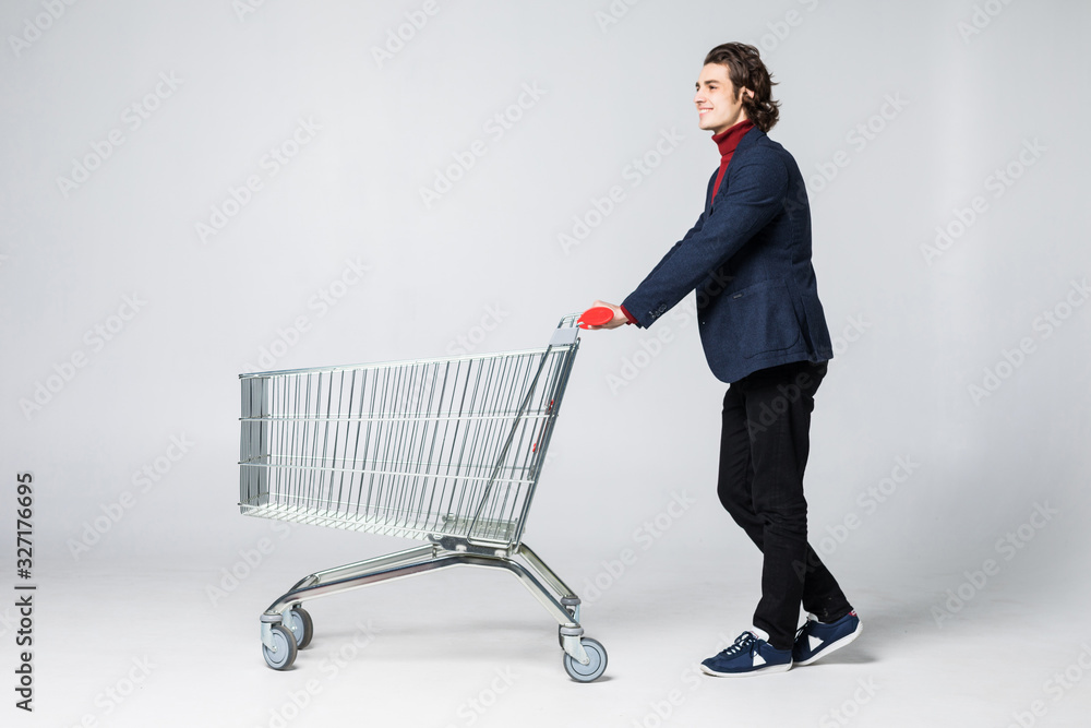 Full length view of handsome young man standing with shopping trolley ...