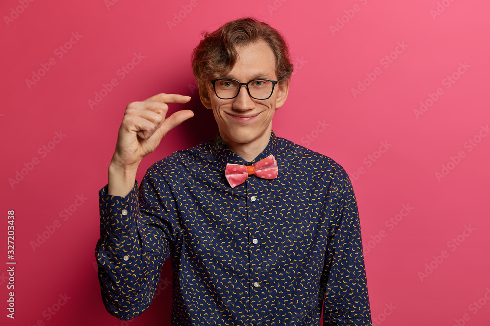 Handsome positive nerd man does small size hand sign with fingers ...