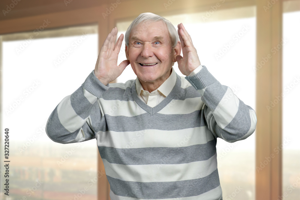 Old man with hands cupped to ears. Funny grandpa in windows background ...