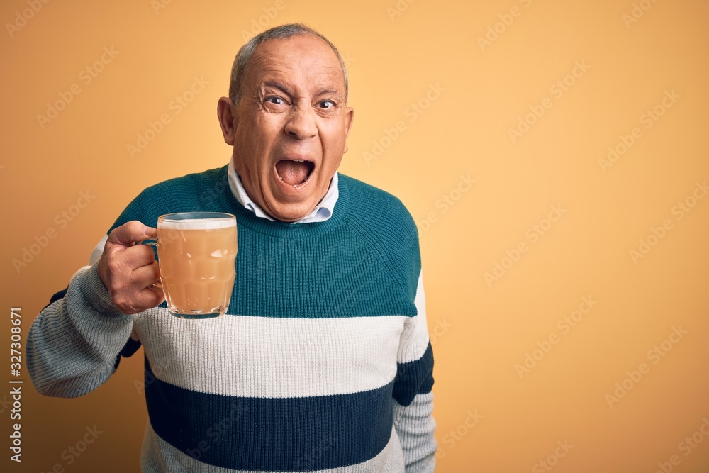 Senior handsome man drinking jar of beer standing over isolated yellow ...