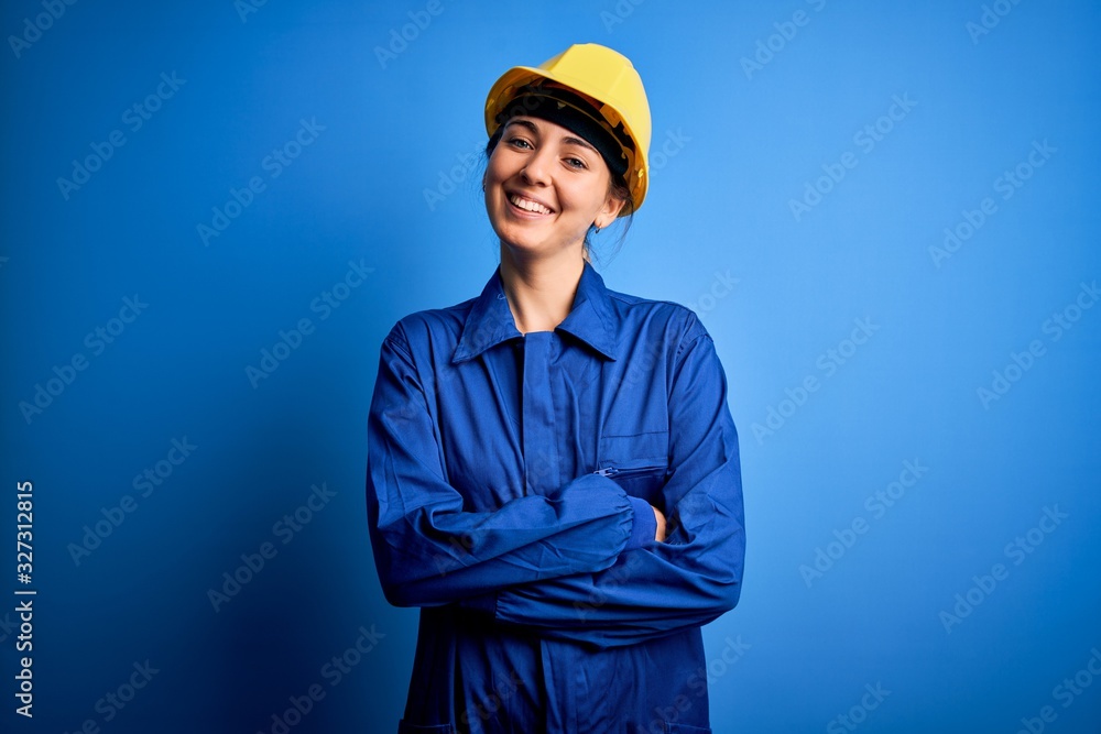 Young beautiful worker woman with blue eyes wearing security helmet and ...