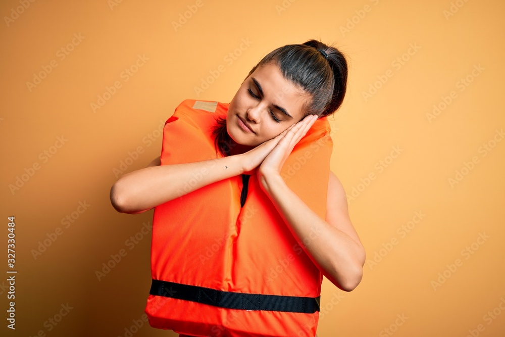 Young beautiful brunette woman wearing orange safe lifejacket over ...