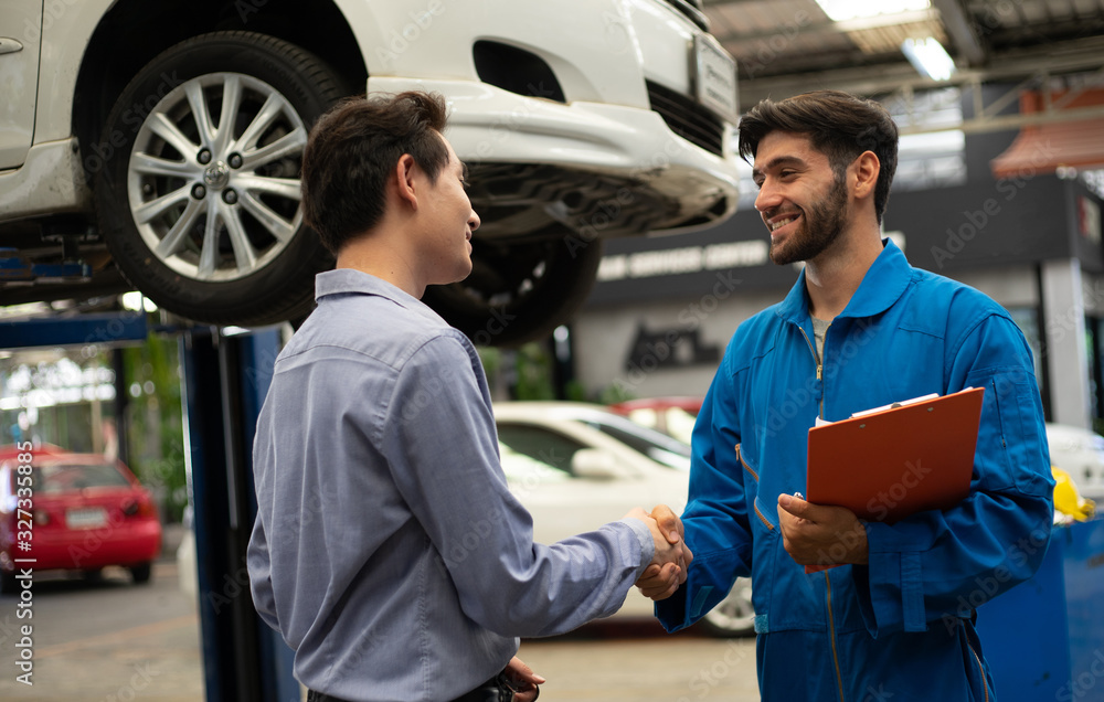 Mechanic holding clipboard shaking hands with car owner in the workshop ...