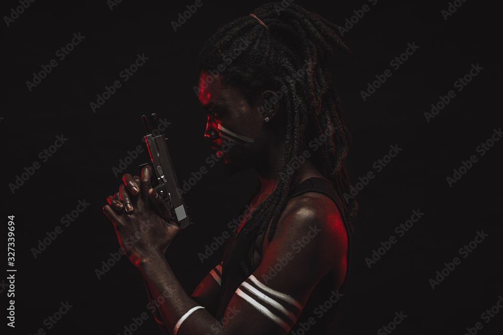 side view on young dreadful african man with gun in hands, he has ...