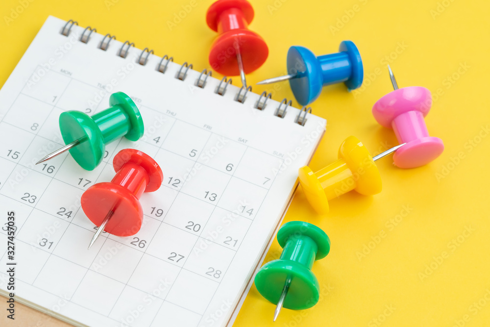 Colorful oversized thumbtack or pushpin on white calendar on yellow ...