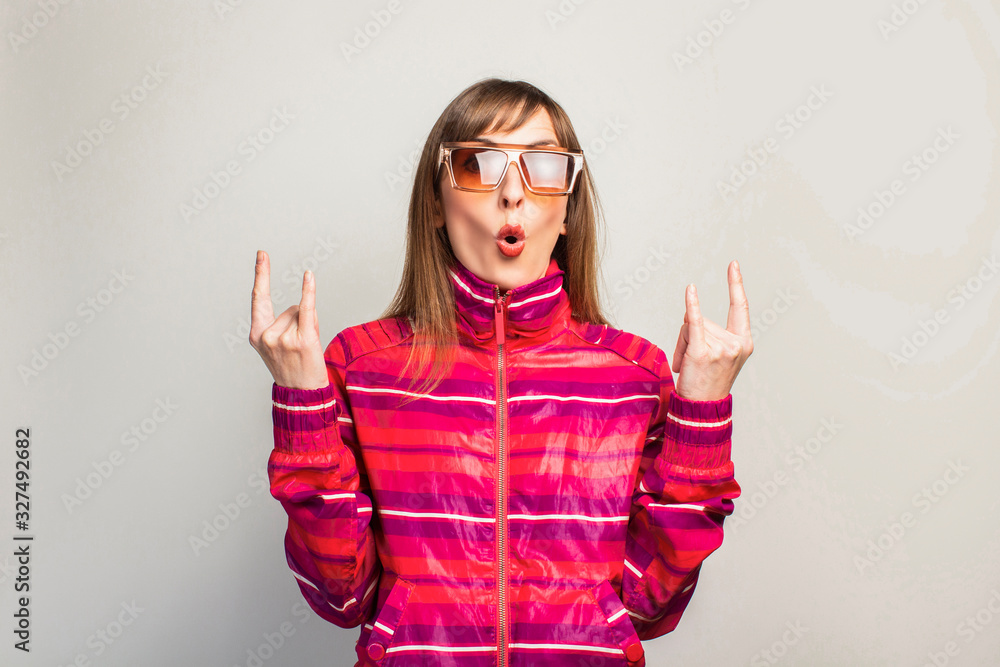 Young woman in a pink sports jacket makes a rock and roll goat gesture ...