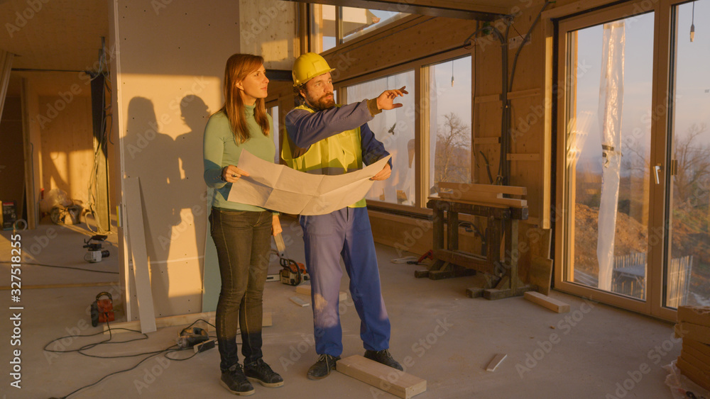 Contractor in overalls shows home owner around the unfinished house at ...