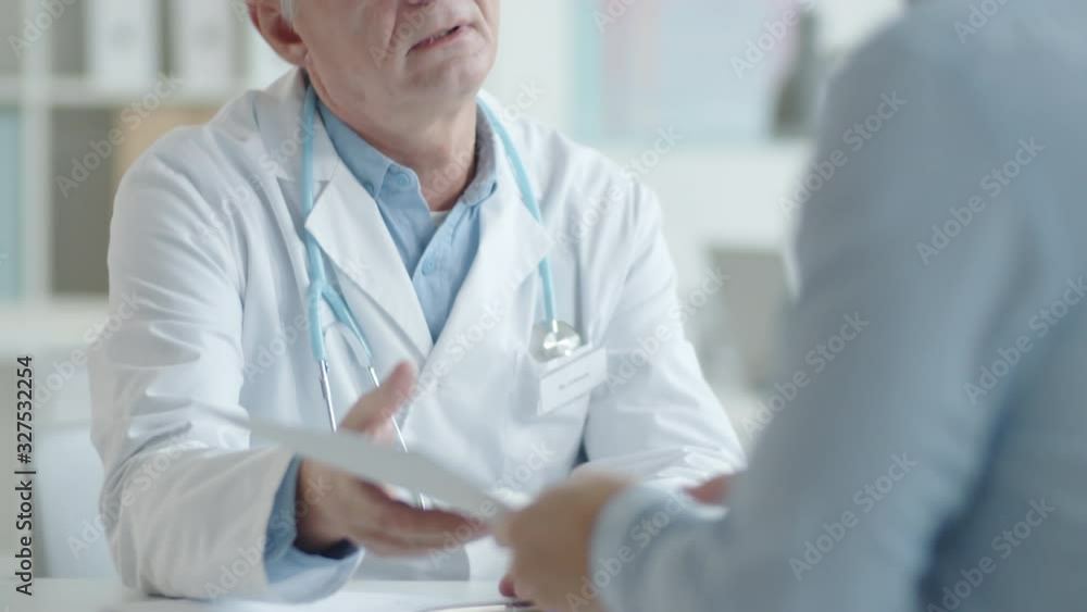 Tilt up of senior doctor giving handshake to male patient, reading his ...