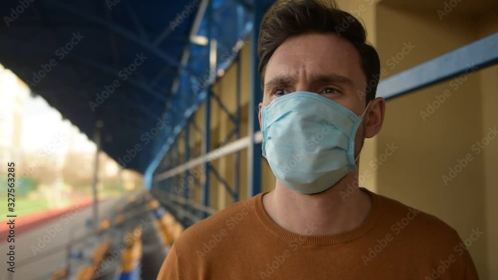 Man in surgical mask standing on empty stadium. Man puts the mask on of ...