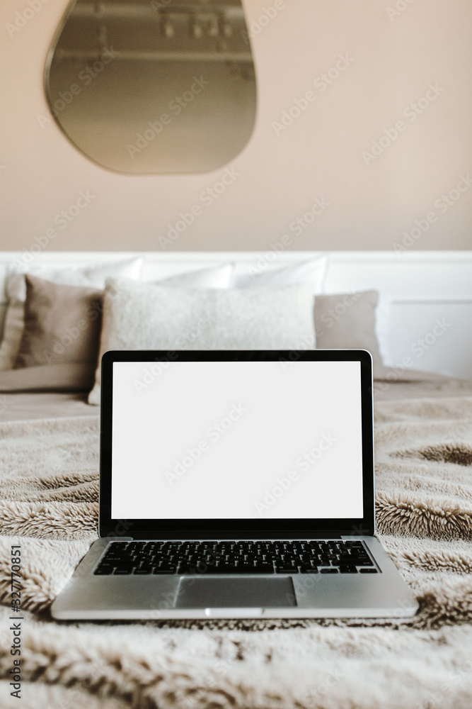 Blank screen laptop on bed with pillows in front of beige wall. Copy ...