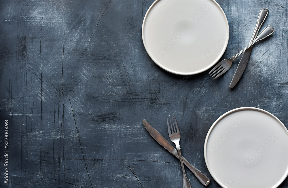 White craft plate, cutlery and napkin on dark stone table. Top view ...