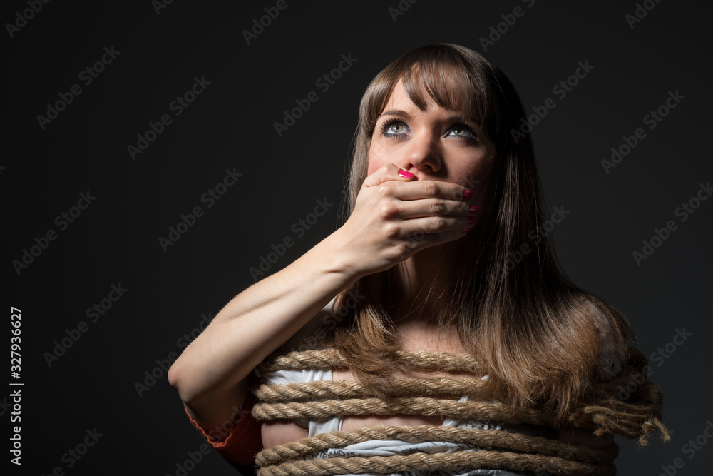 Front view of female victim being tied up with rope and muted by hand. Lady hand covering mouth ...