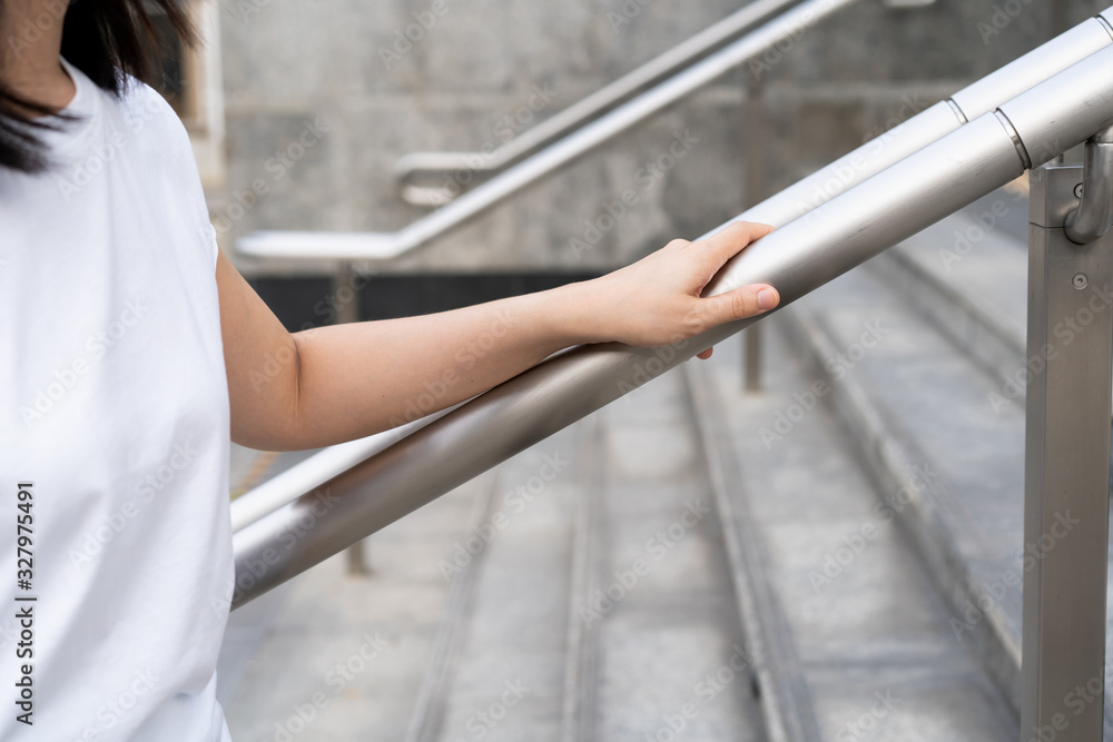 Woman walking on the stair way and grabbing on safety stair rail. Close ...