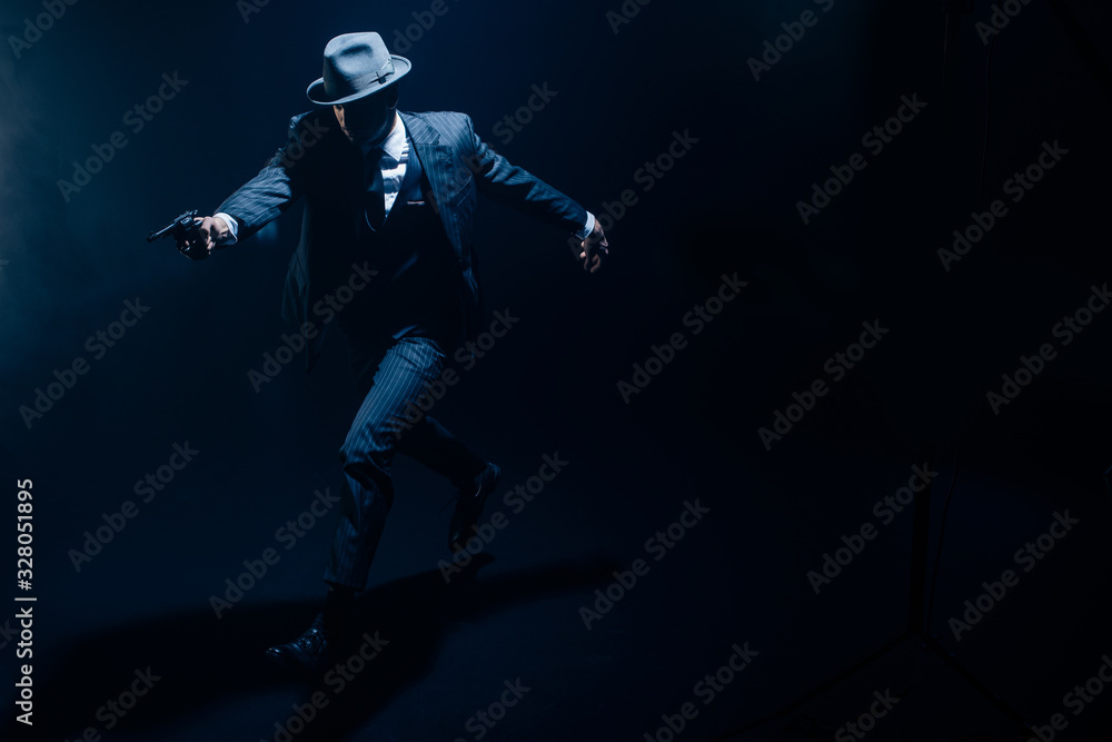 Gangster with outstretched hand aiming revolver and running on dark ...
