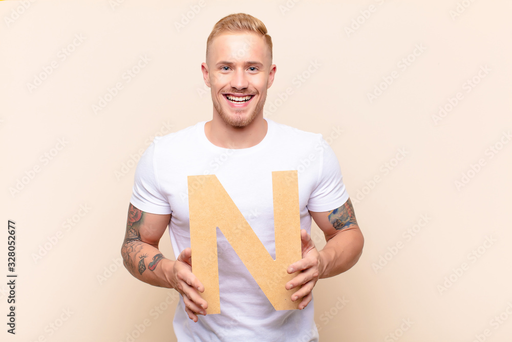 young blonde man excited, happy, joyful, holding the letter N of the ...